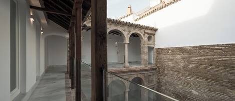 Um corredor com guarda-corpo de vidro, arcos de pedra e piso de azulejos.