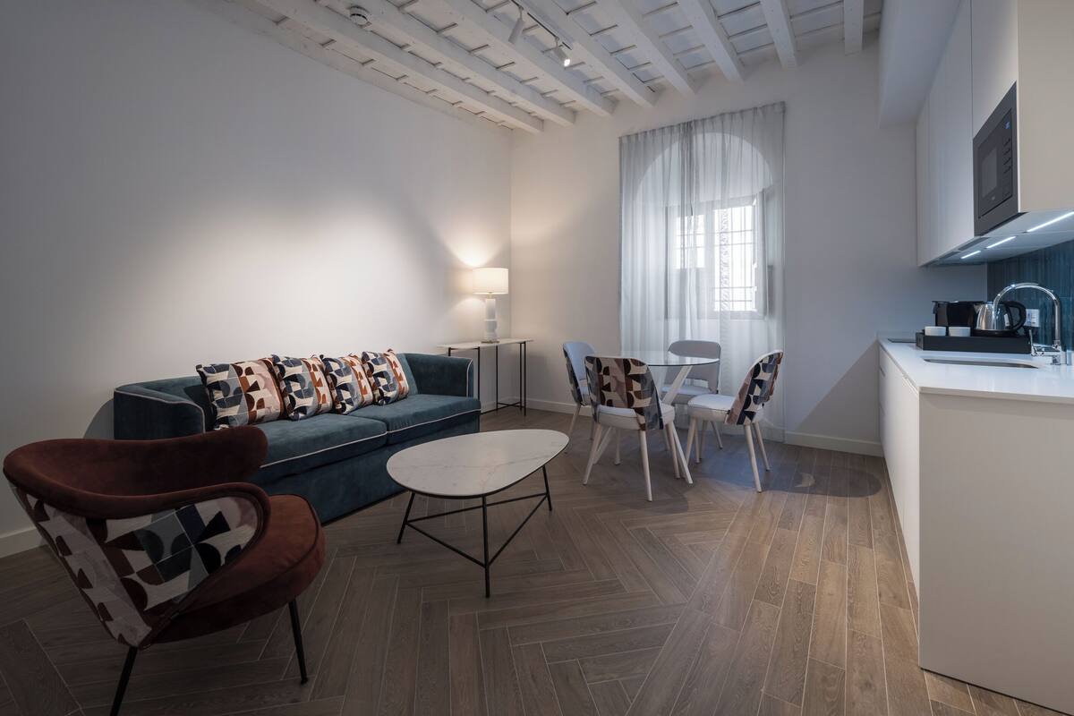 Uma sala de estar moderna com um sofá, duas poltronas, uma mesa de centro e uma área de jantar com cadeiras e uma mesa.
