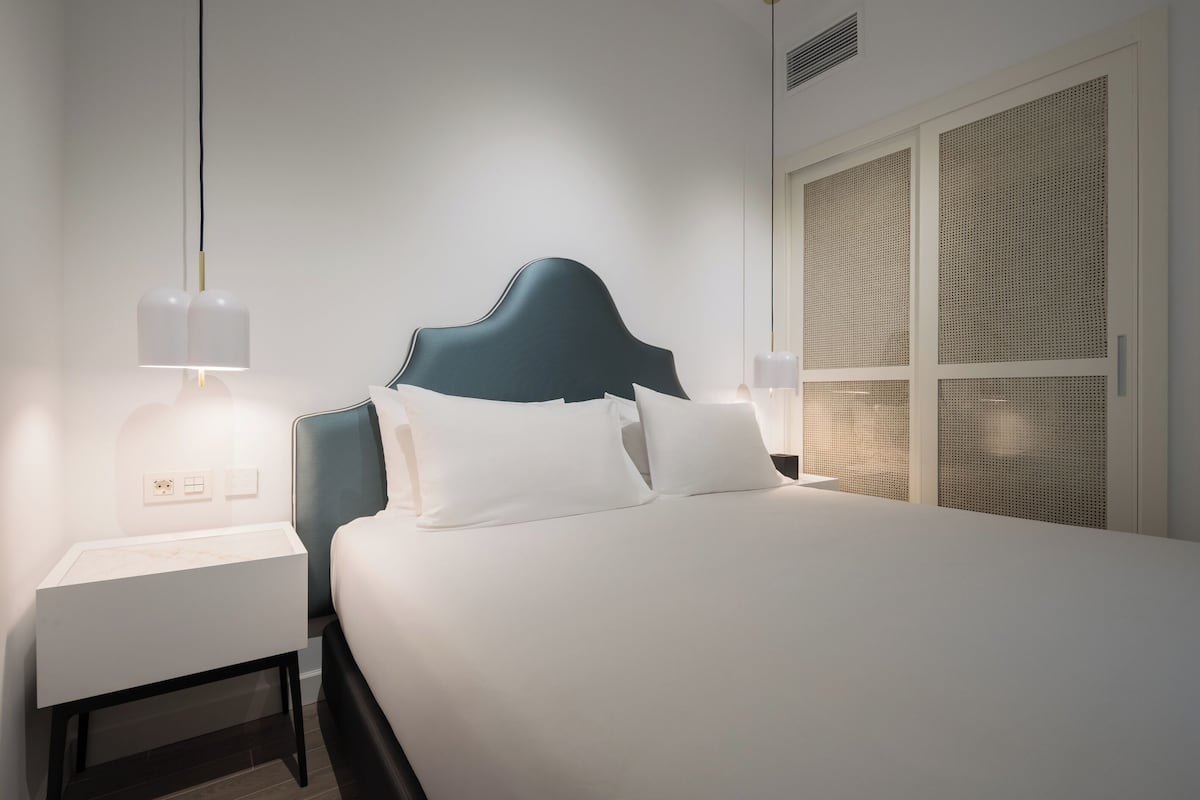 Quarto moderno com cama, mesas de cabeceira e janela com persiana estampada.