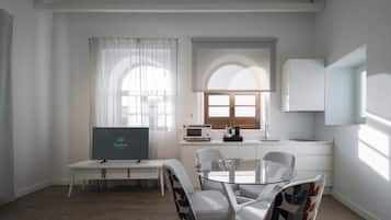 Um quarto moderno e bem iluminado com mesa de jantar, cadeiras, televisão, micro-ondas e janela com cortinas.