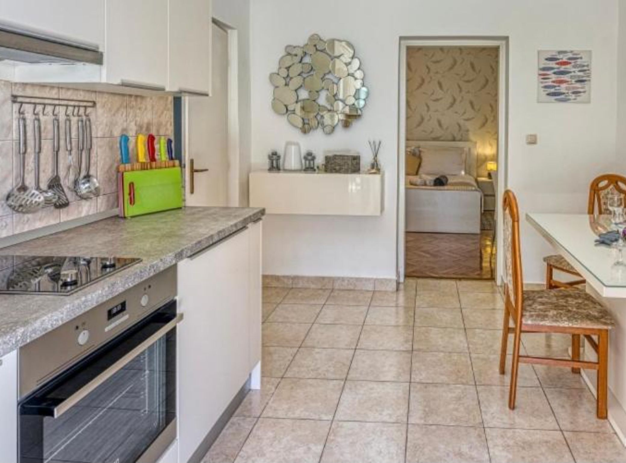 Uma cozinha moderna com fogão embutido, sala de jantar com mesa e cadeiras, e um painel decorativo na parede.