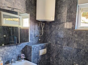 Um banheiro com azulejos de mármore escuro, um espelho grande, um vaso sanitário suspenso e uma área de chuveiro.