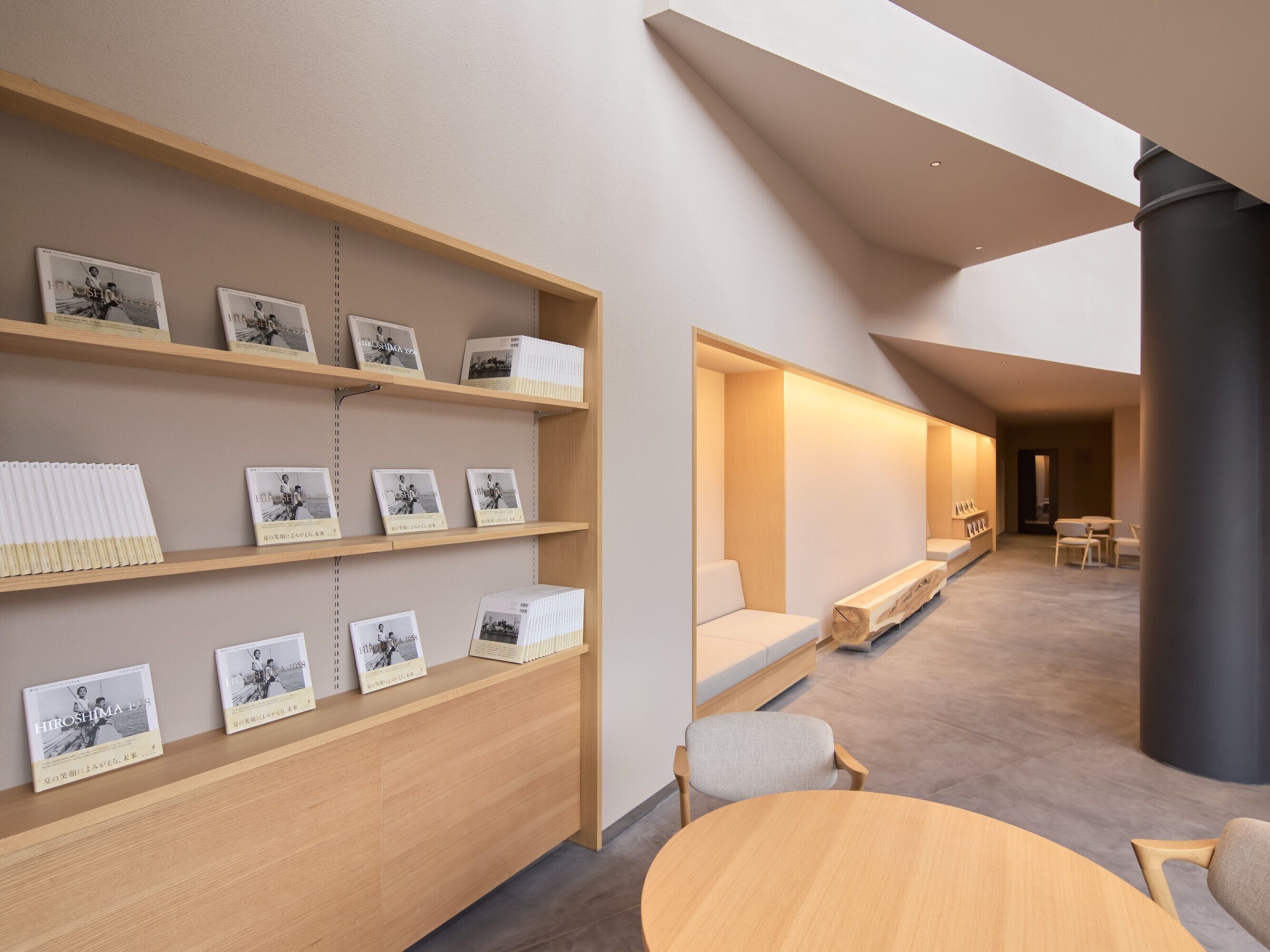 Um interior moderno com estantes de madeira exibindo livros e fotografias emolduradas, uma mesa redonda e um espaço de estar com um banco.