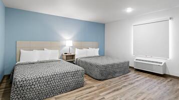 Quarto de hotel com duas camas, uma mesa de cabeceira, um abajur e ar-condicionado fixado na parede.