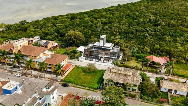 Vista aérea de uma cidade costeira com mistura de edifícios modernos e tradicionais, uma grande massa de água e vegetação exuberante.