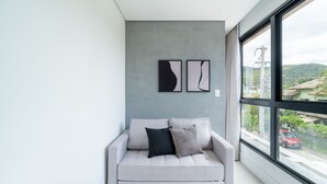 Uma sala de estar moderna com um sofá cinzento, duas obras de arte abstratas nas paredes e uma janela grande com vista para a paisagem urbana.