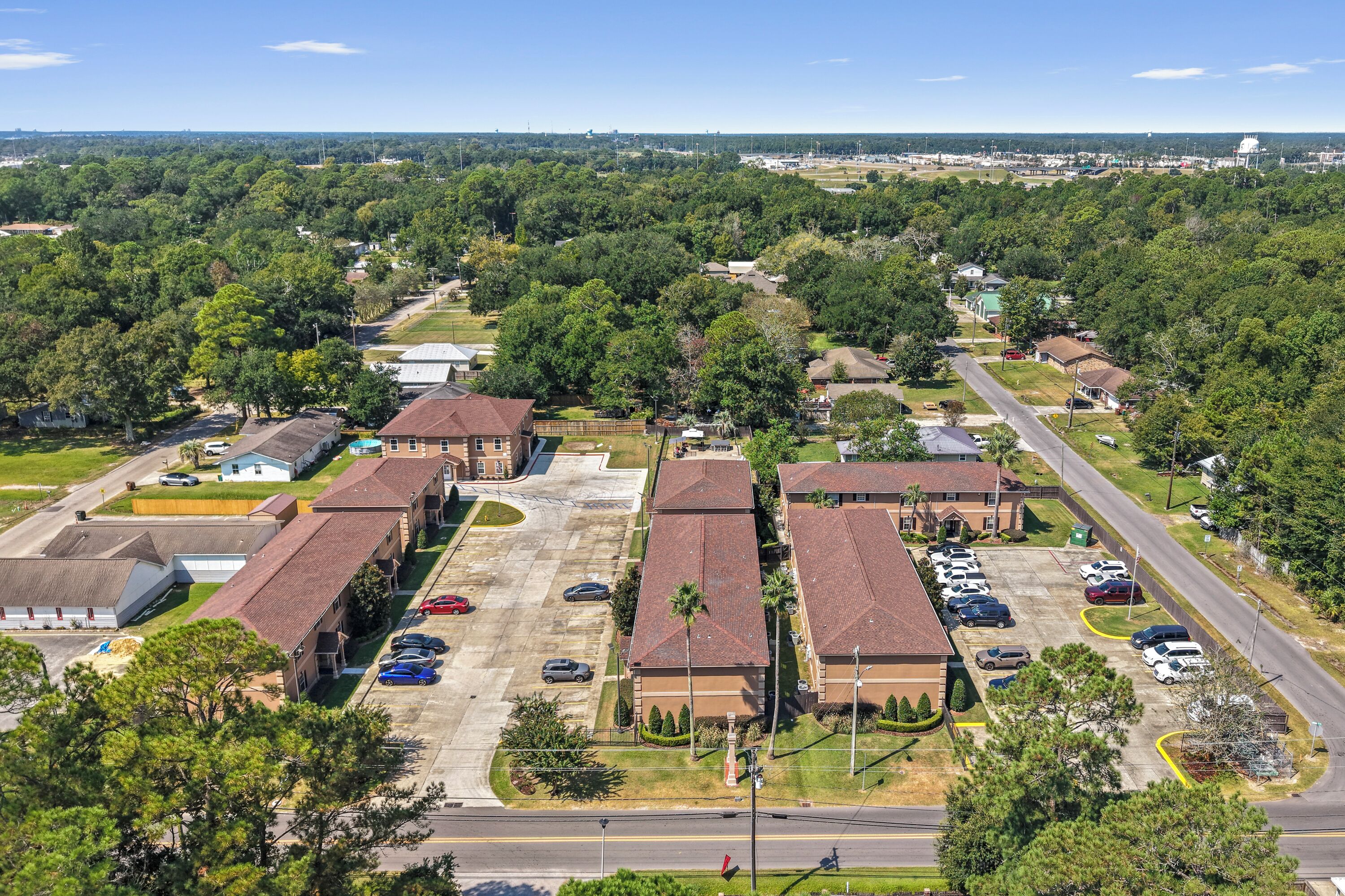 Vista aérea de uma área residencial com vários edifícios, um estacionamento e vegetação ao redor.