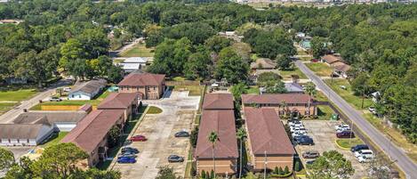 Vista aérea de uma área residencial com vários edifícios, um estacionamento e vegetação ao redor.