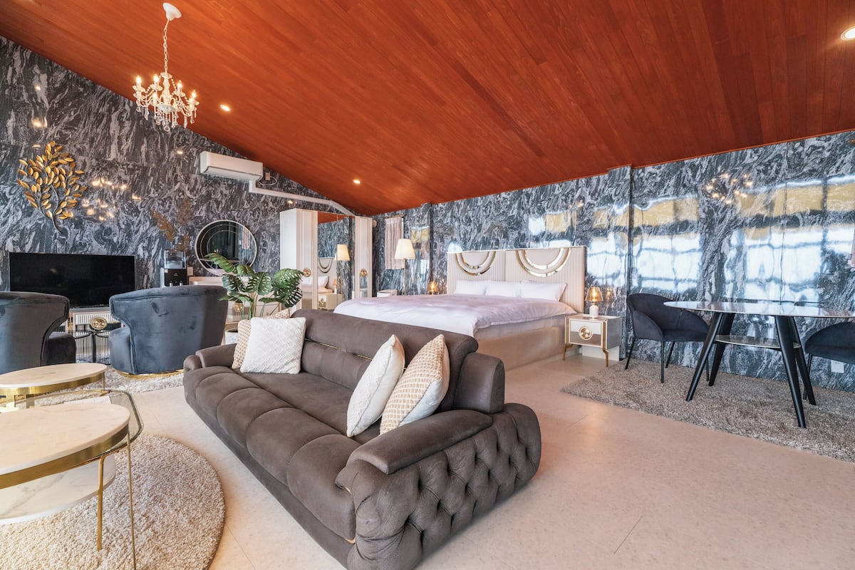 Quarto moderno com cama grande, sofá, TV e área de jantar.