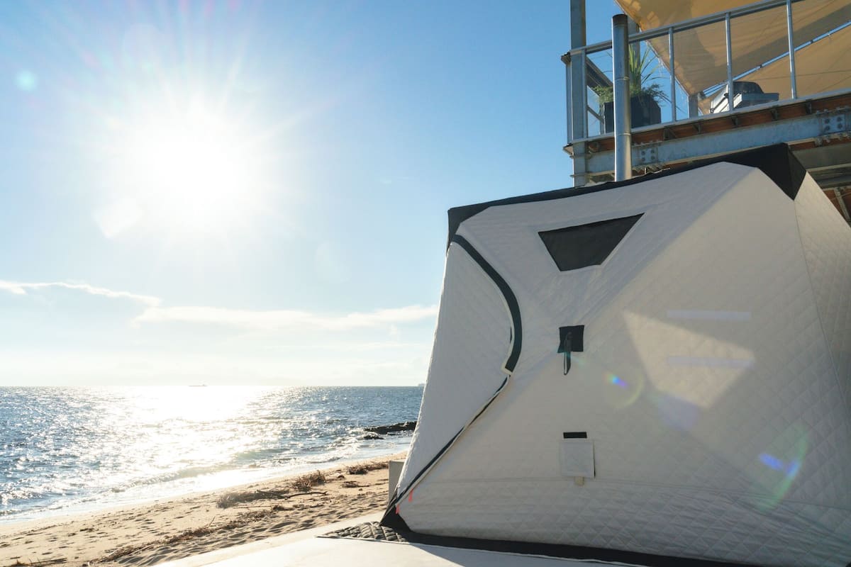 Uma tenda numa praia com céu claro e o sol brilhando.