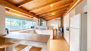 Cozinha moderna com vigas de madeira, uma ilha grande com banquetas e vista para o exterior.