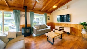 Uma sala de estar acolhedora com teto de madeira, lareira, sofá, mesa de centro e televisão na parede.