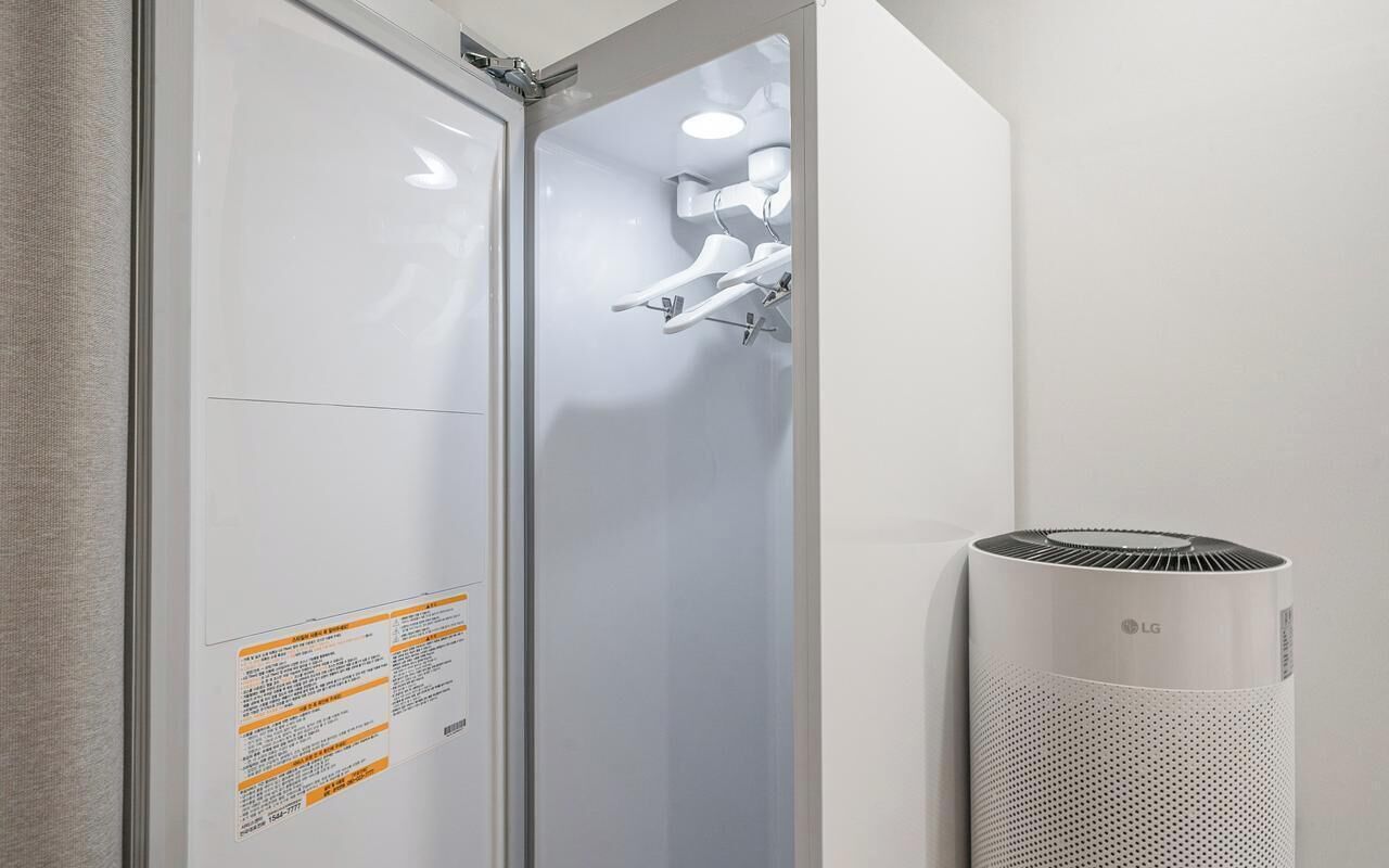 Casa de banho com chuveiro em cabine de vidro, secador de cabelo fixado na parede e aquecedor vertical.