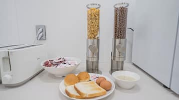 Uma cozinha com uma torradeira, dois distribuidores de alimentos, um prato de cereais, uma fatia de pão com ovos e uma tigela de leite.