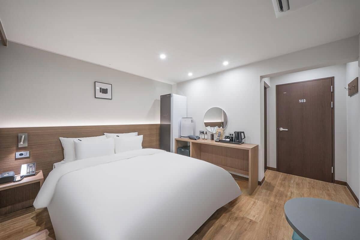 Quarto de hotel com uma cama grande, uma mesa com computador, um guarda-roupa e uma porta com a identificação 503.