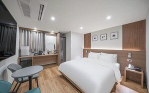 Quarto de hotel moderno com uma cama grande, uma mesa com cadeira, uma mesinha, um espelho e uma mesinha de cabeceira com telefone.