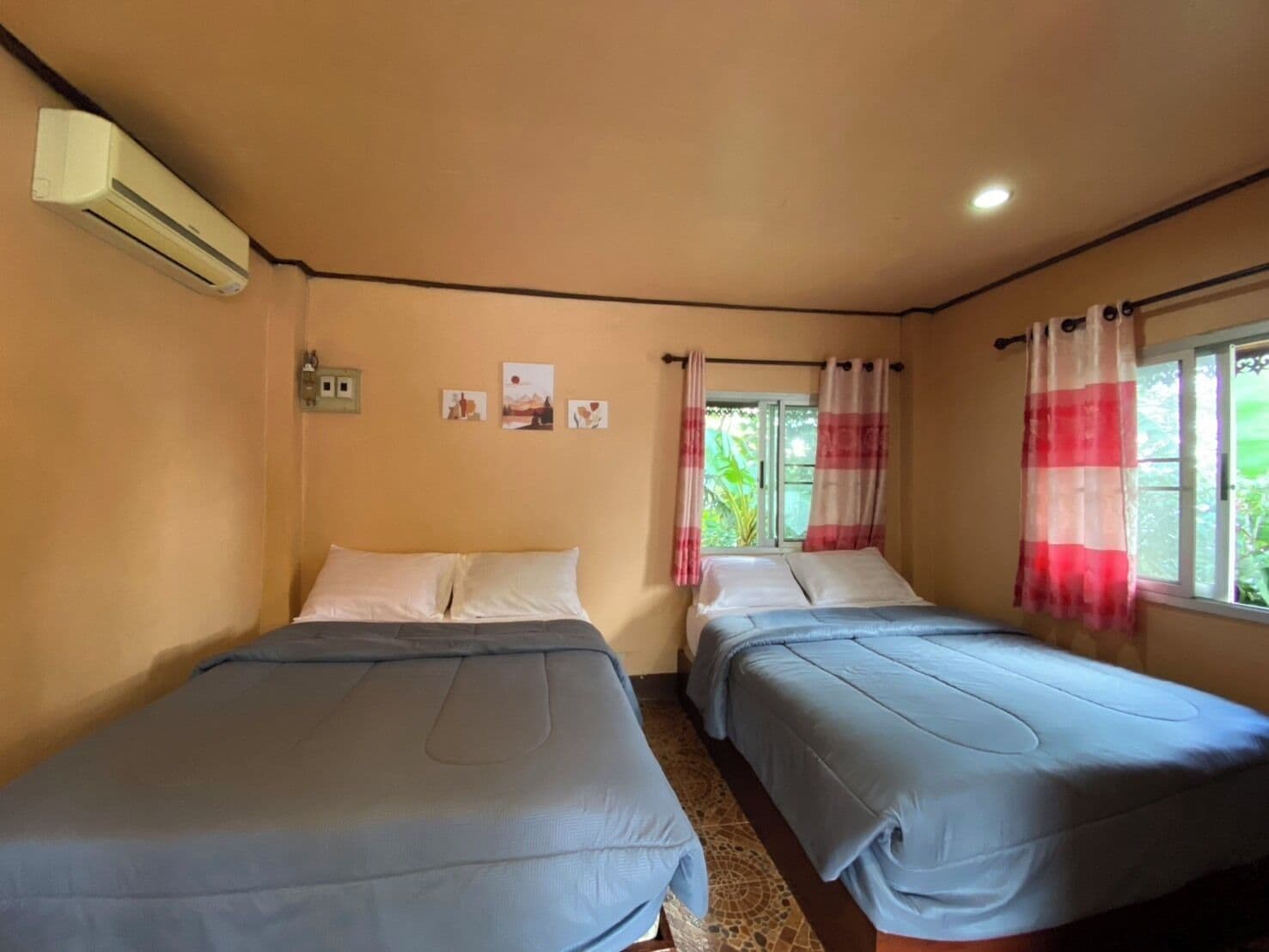 Quarto com duas camas, paredes bege e uma janela com cortinas.
