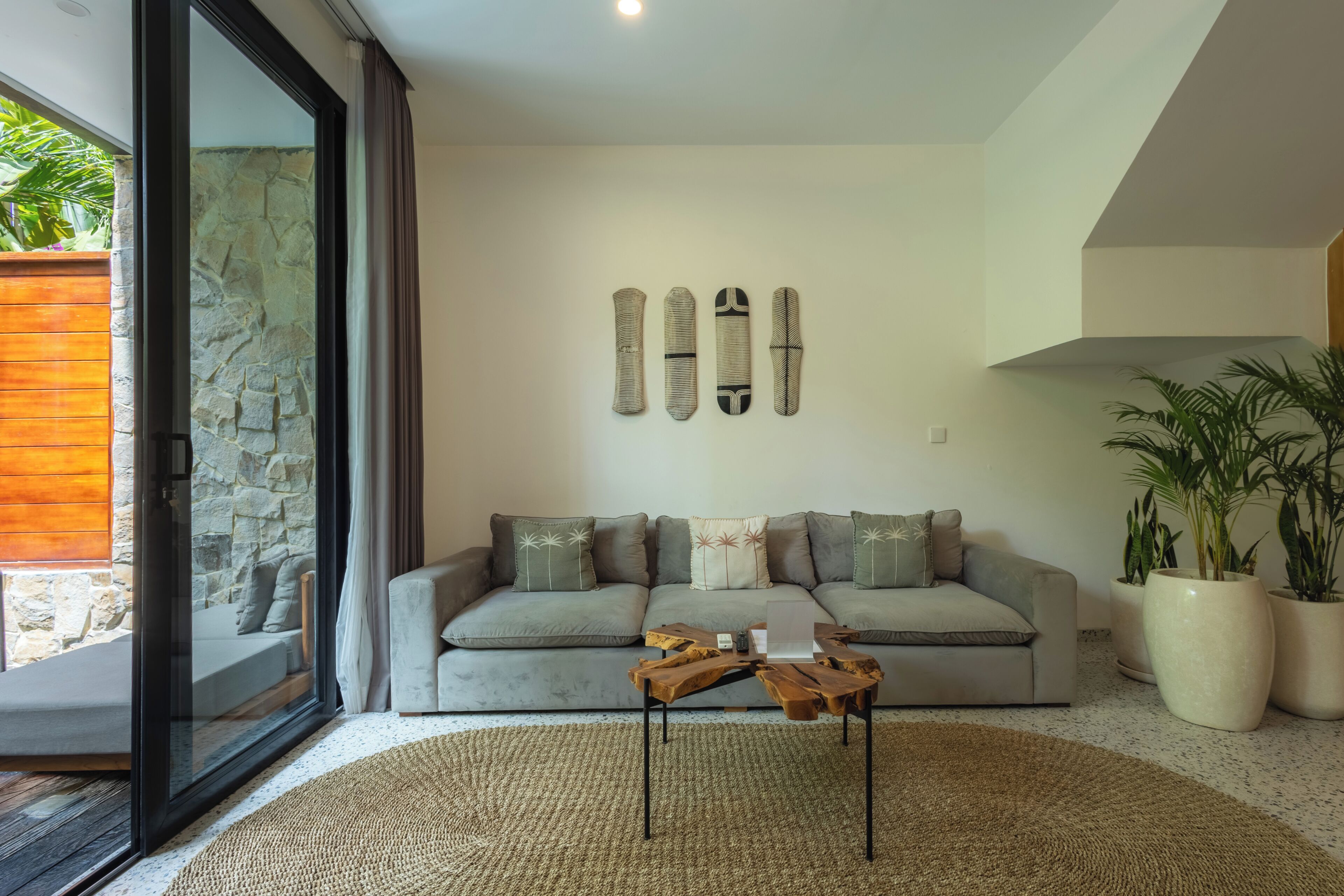 Uma sala de estar moderna com um sofá cinzento, uma mesa de centro de madeira e uma parede de pedra.