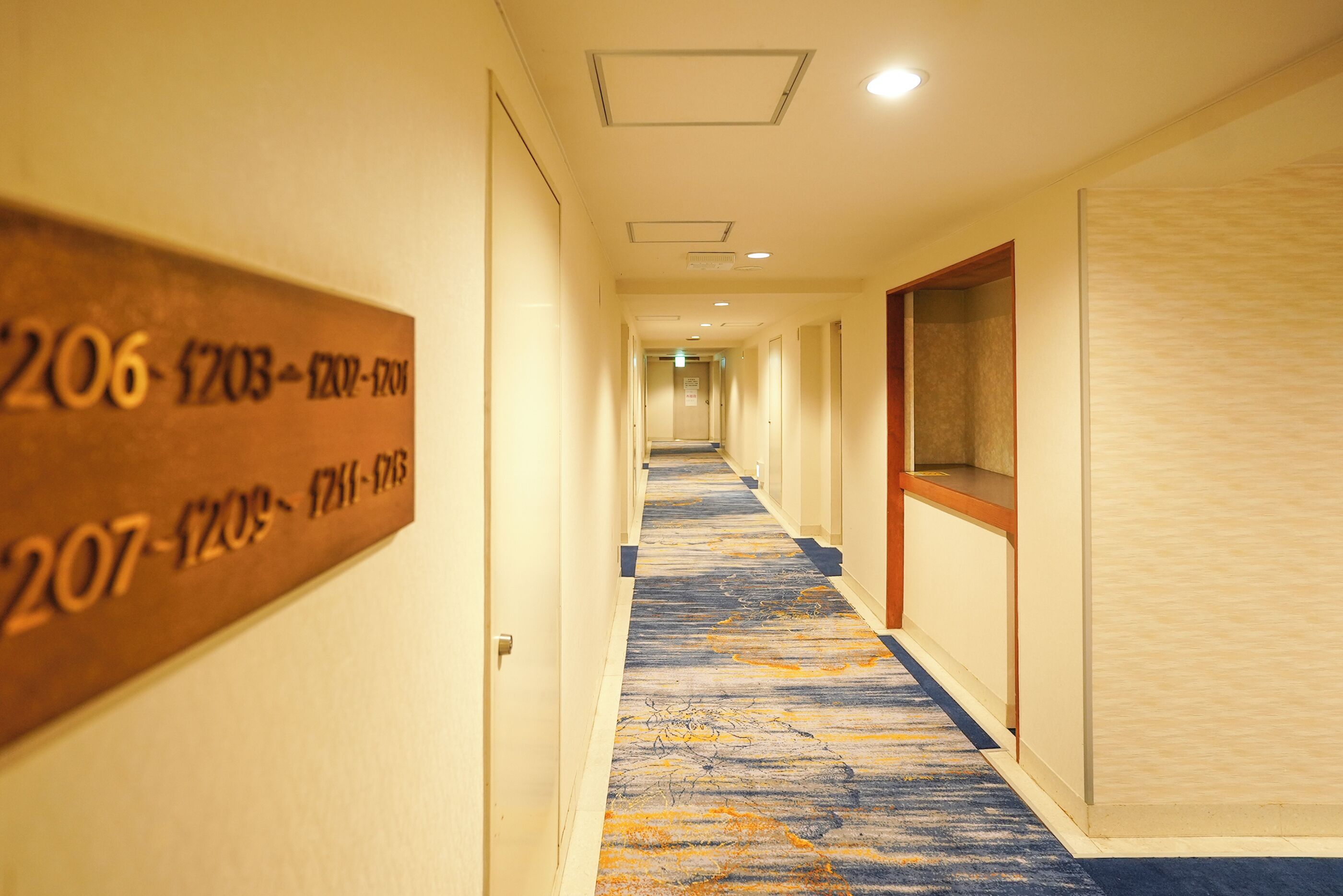 Um corredor de hotel com piso em carpete e portas identificadas com números de quarto.