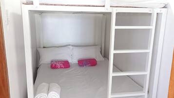 Quarto com uma cama individual, beliche branco, duas almofadas e um pequeno prateleira.