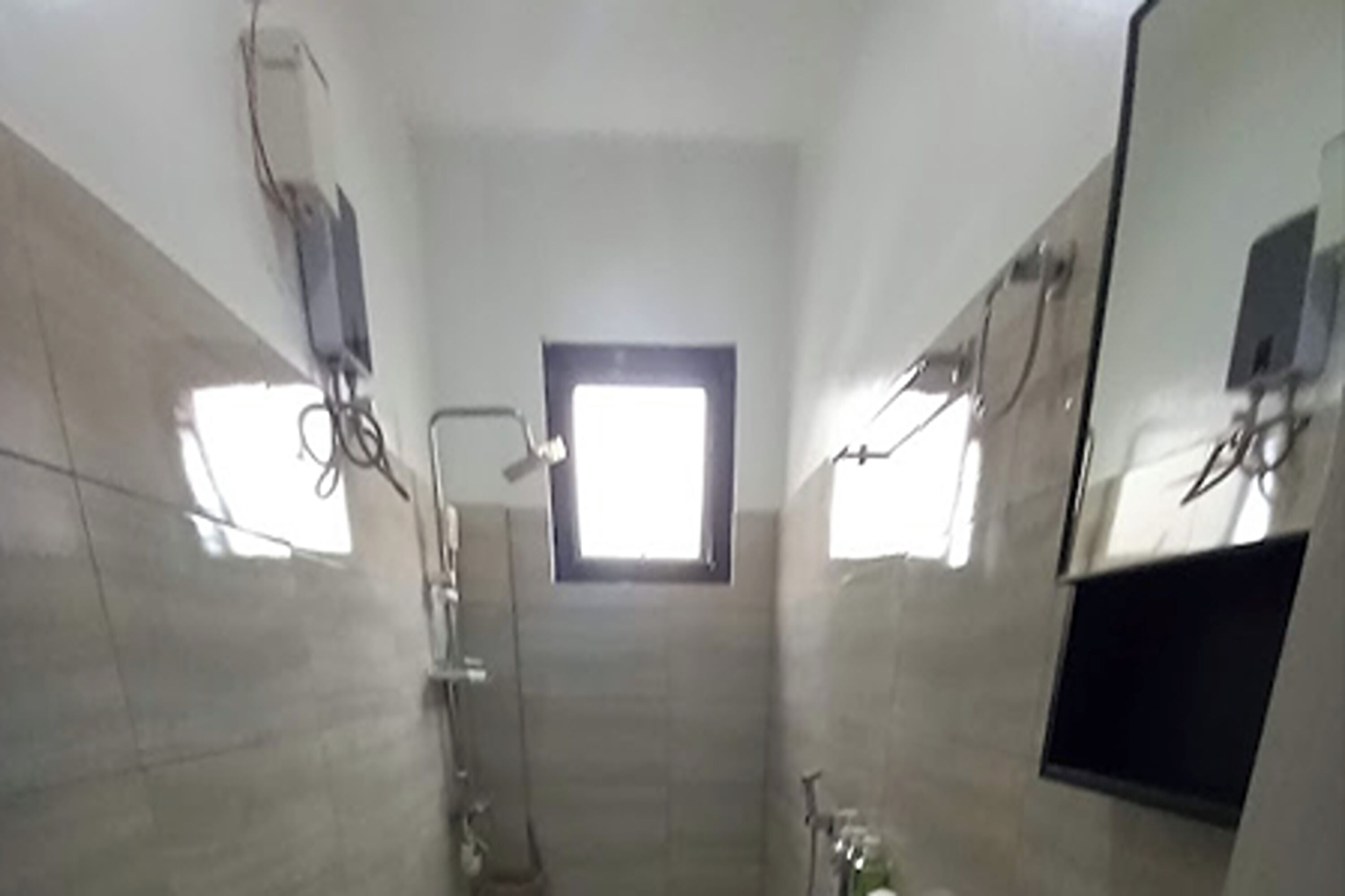 Casa de banho com paredes em azulejo, uma janela e um espelho.