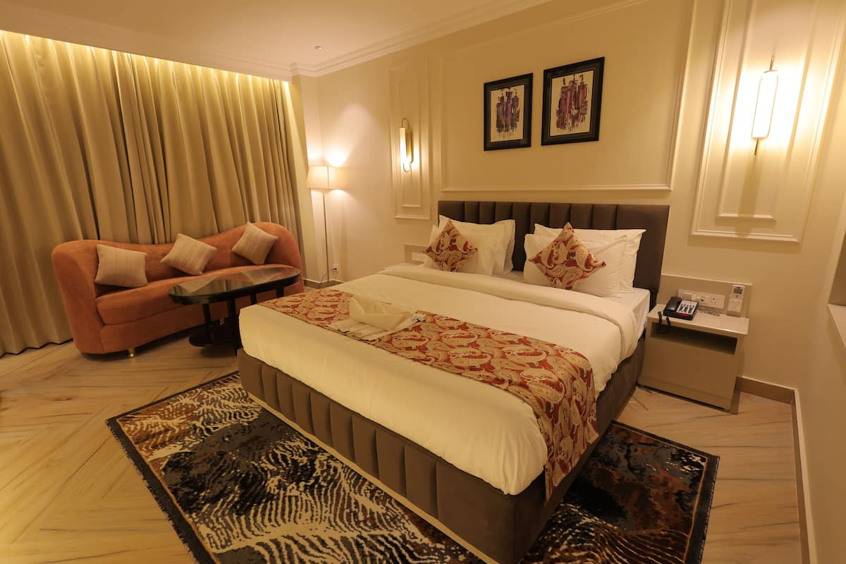 Quarto de hotel com cama, sofá, mesa de cabeceira e luminária.