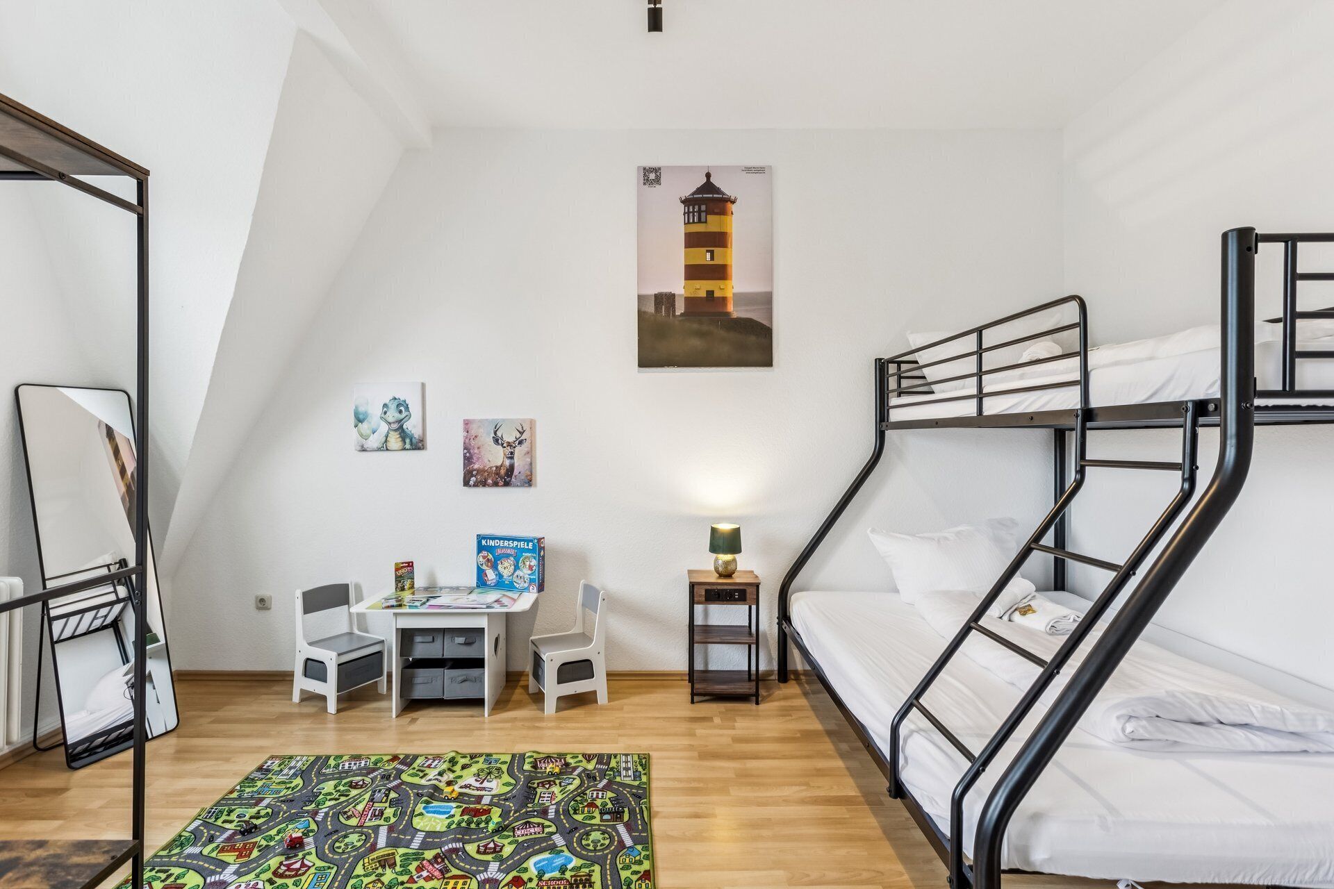 Um quarto de dormitório com beliches, escrivaninha, cadeiras, luminária e um quadro com um farol.