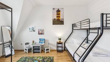 Um quarto de dormitório com beliches, escrivaninha, cadeiras, luminária e um quadro com um farol.