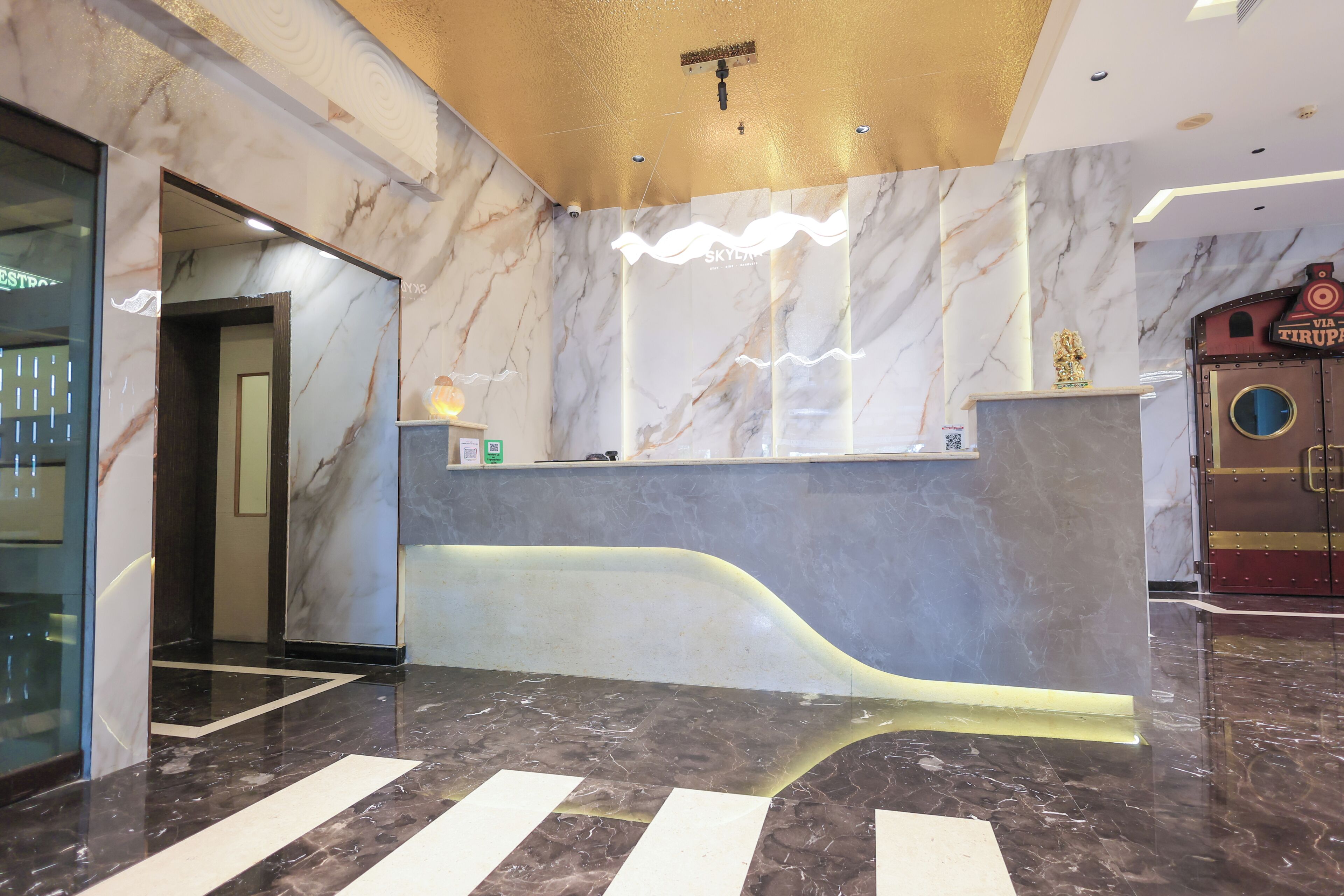 Uma área de recepção com balcão de mármore, teto dourado e máquina de check-in.