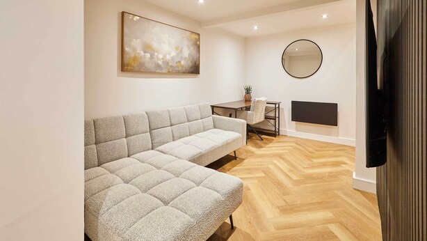 Uma sala de estar moderna com um sofá cinzento, um espelho redondo e uma televisão de tela plana fixada na parede.