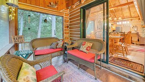 Interior de cabana de troncos com móveis de vime, área de jantar e vista para a floresta.