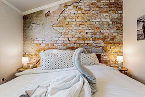 Quarto de hotel com parede de tijolos, cama com roupa de cama branca e duas luminárias de cabeceira.