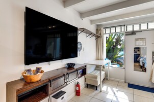 Uma sala de estar moderna com uma televisão de tela plana grande, console de madeira, sofá branco e uma janela com vista para o verde.