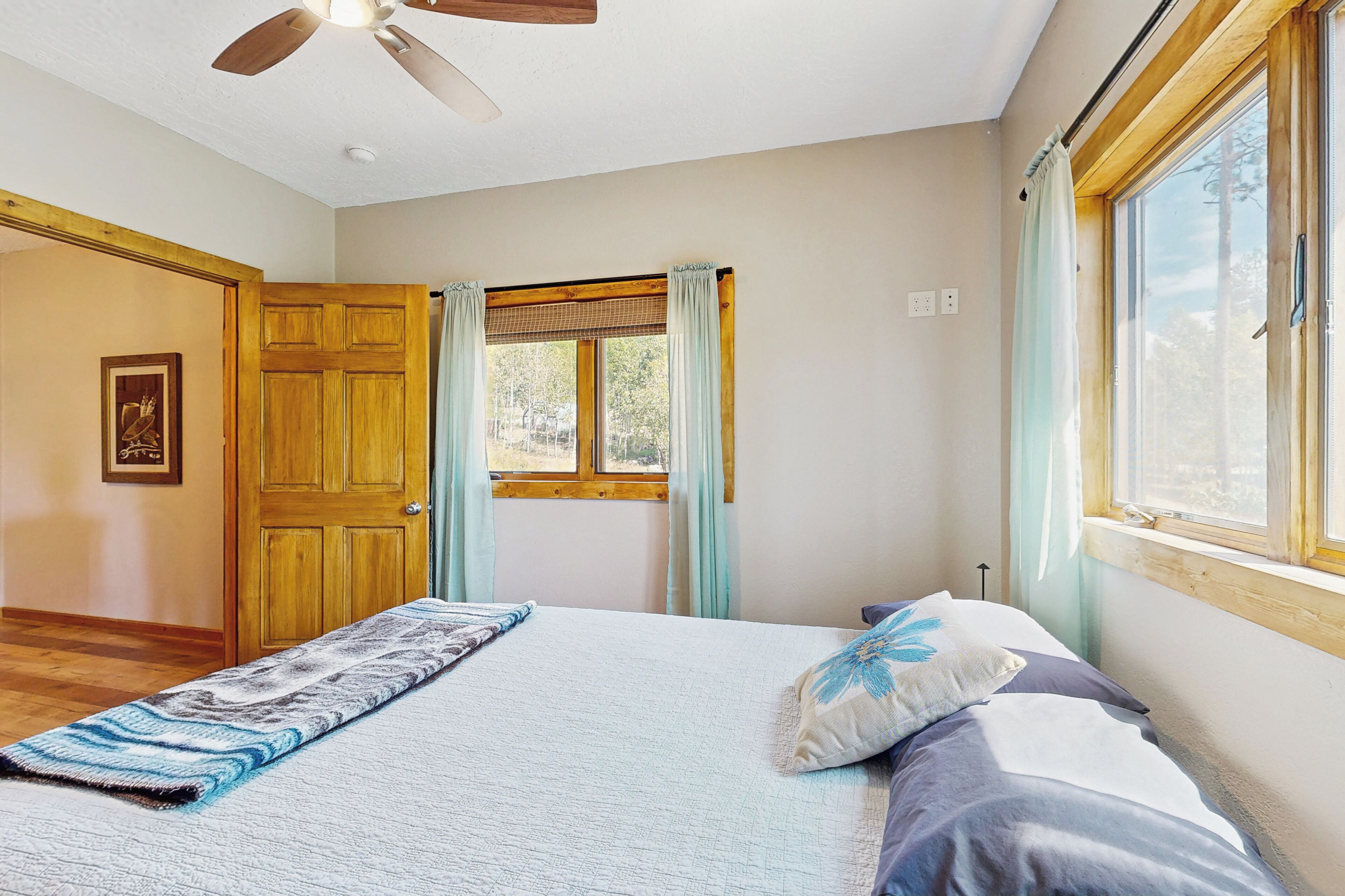Quarto com cama, ventoinha no teto, janela com cortinas e porta de madeira.