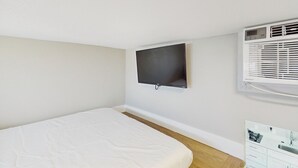 Quarto com cama, TV fixada na parede e aparelho de ar condicionado.