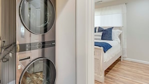 Quarto pequeno com cama, máquina de lavar e espelho.