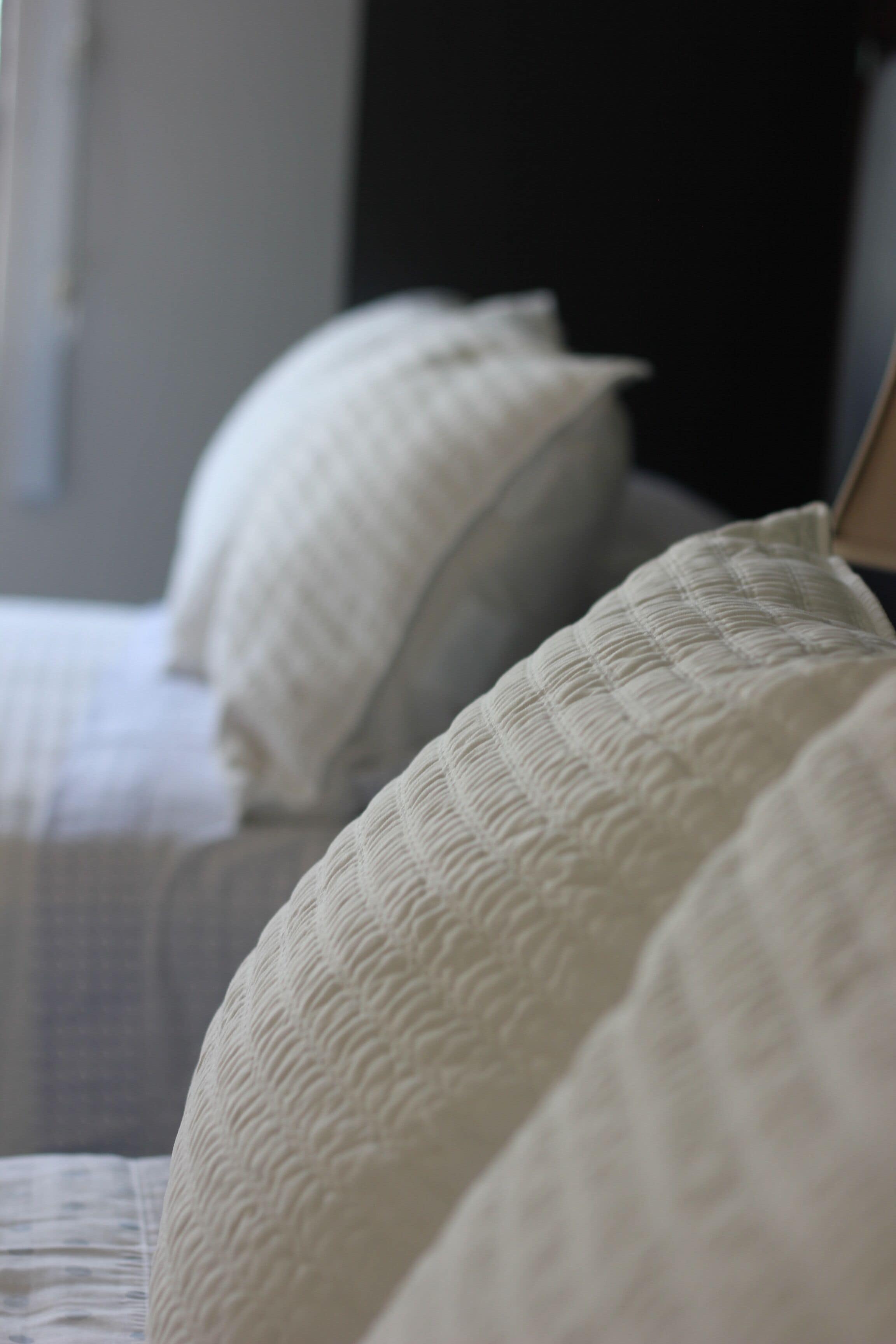 Close-up de uma cama com roupa de cama branca texturizada.