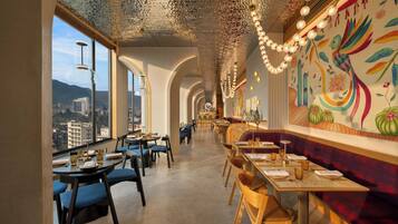 Um restaurante com mesas e cadeiras, um mural na parede e vista para a cidade.