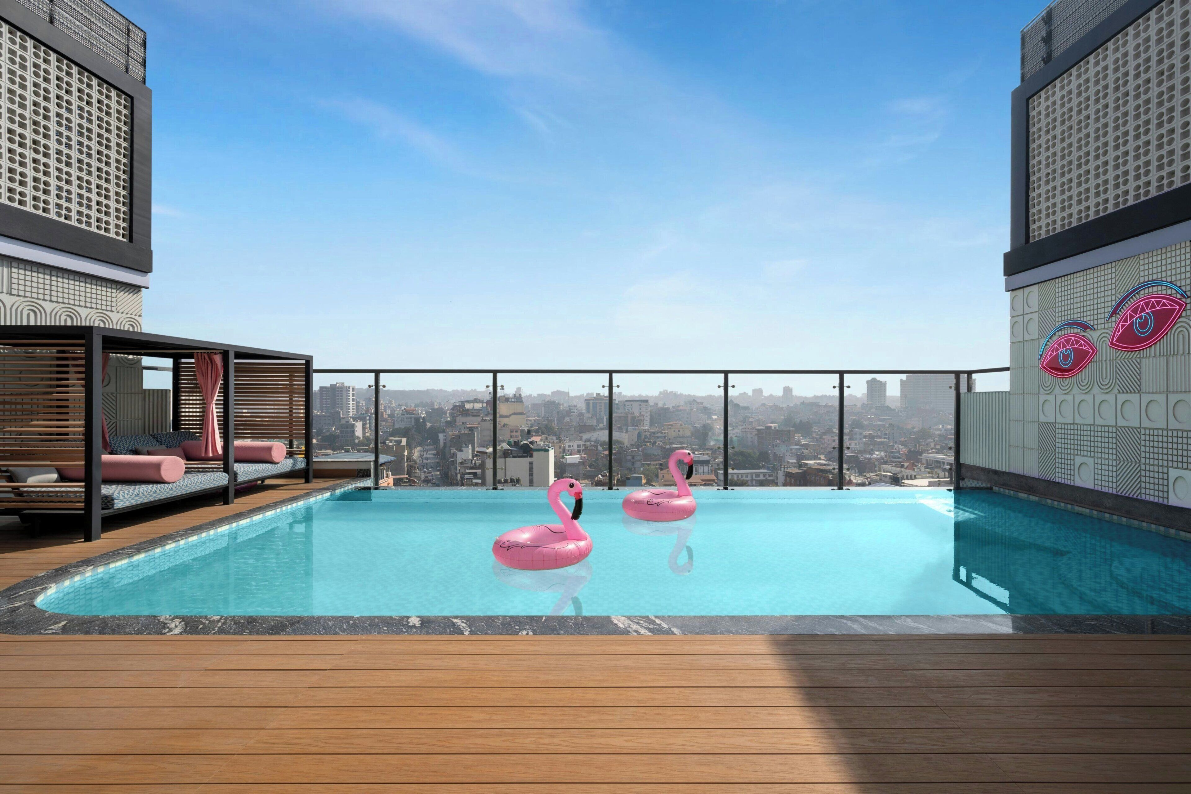 Piscina no terraço com boias em formato de flamingos rosa, vista da cidade e design arquitetônico moderno.