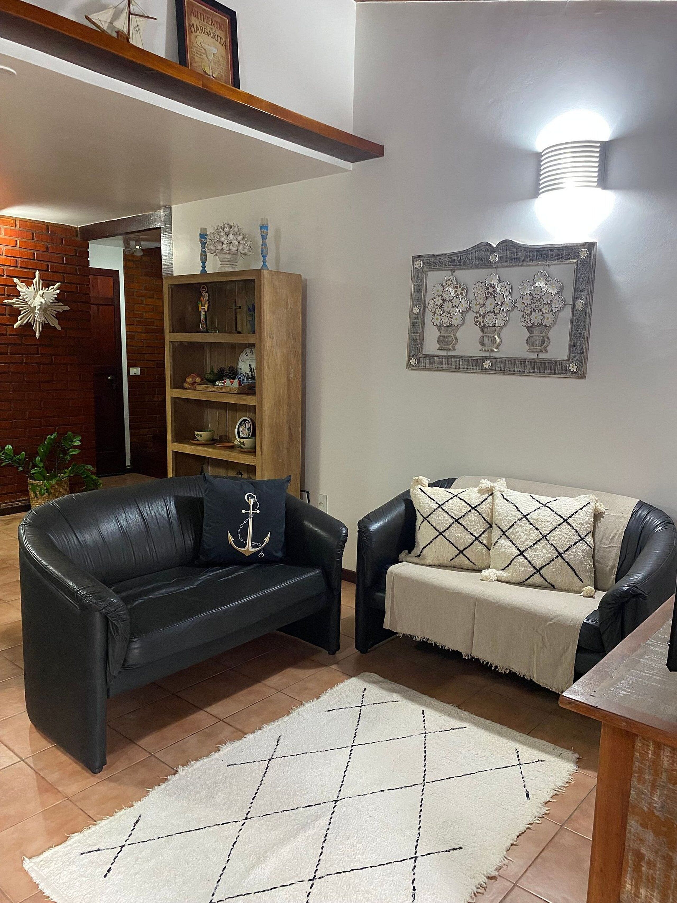 Uma sala de estar com dois sofás, uma estante de madeira, um tapete branco e um ponto de luz fixado na parede.