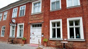 A red brick building with a sign reading "Hotel zum Hofmader." There are two outdoor tables with chairs, and a red rope barrier is visible.