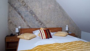 Quarto com parede de pedra, estrutura de cama de madeira, duas mesas de cabeceira com luminárias e um cobertor estampado.