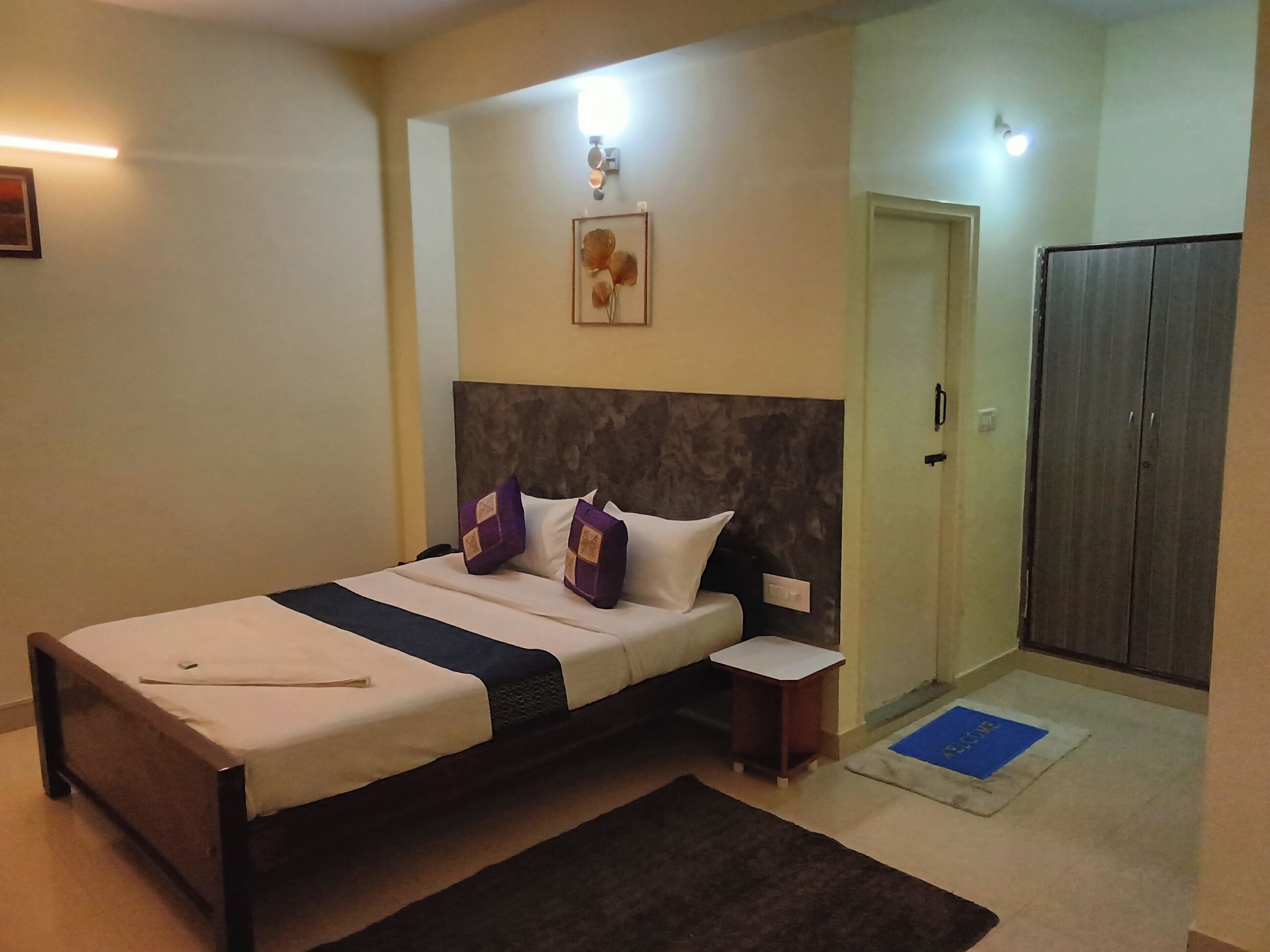 Quarto com cama, mesa de cabeceira, guarda-roupa e luminária na parede.