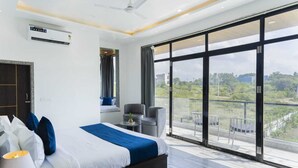 Quarto de hotel moderno com uma cama grande, área de estar e varanda com vista para a cidade.