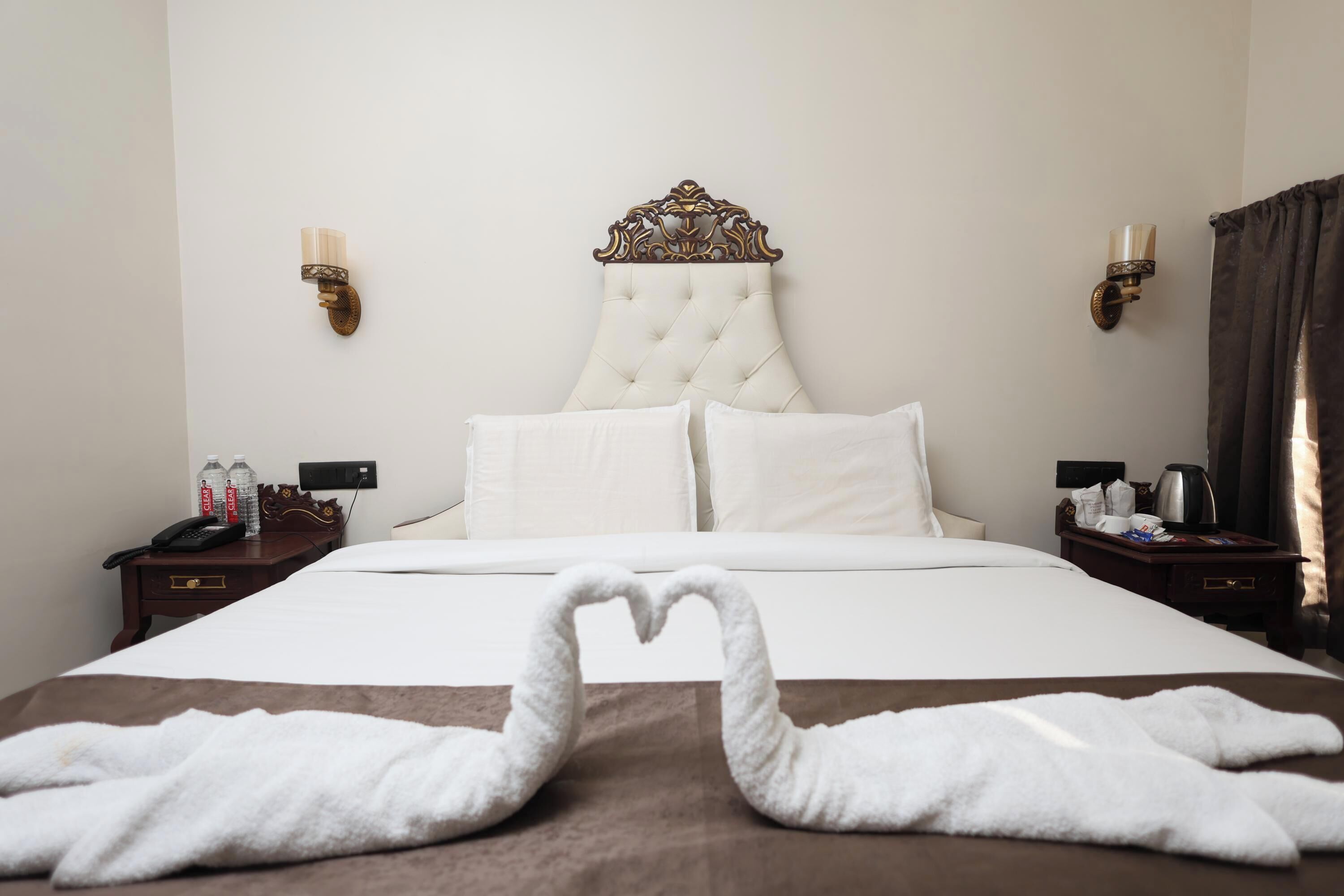Quarto de hotel com cama grande, duas mesas de cabeceira, luminária na parede e cabeceira decorativa.