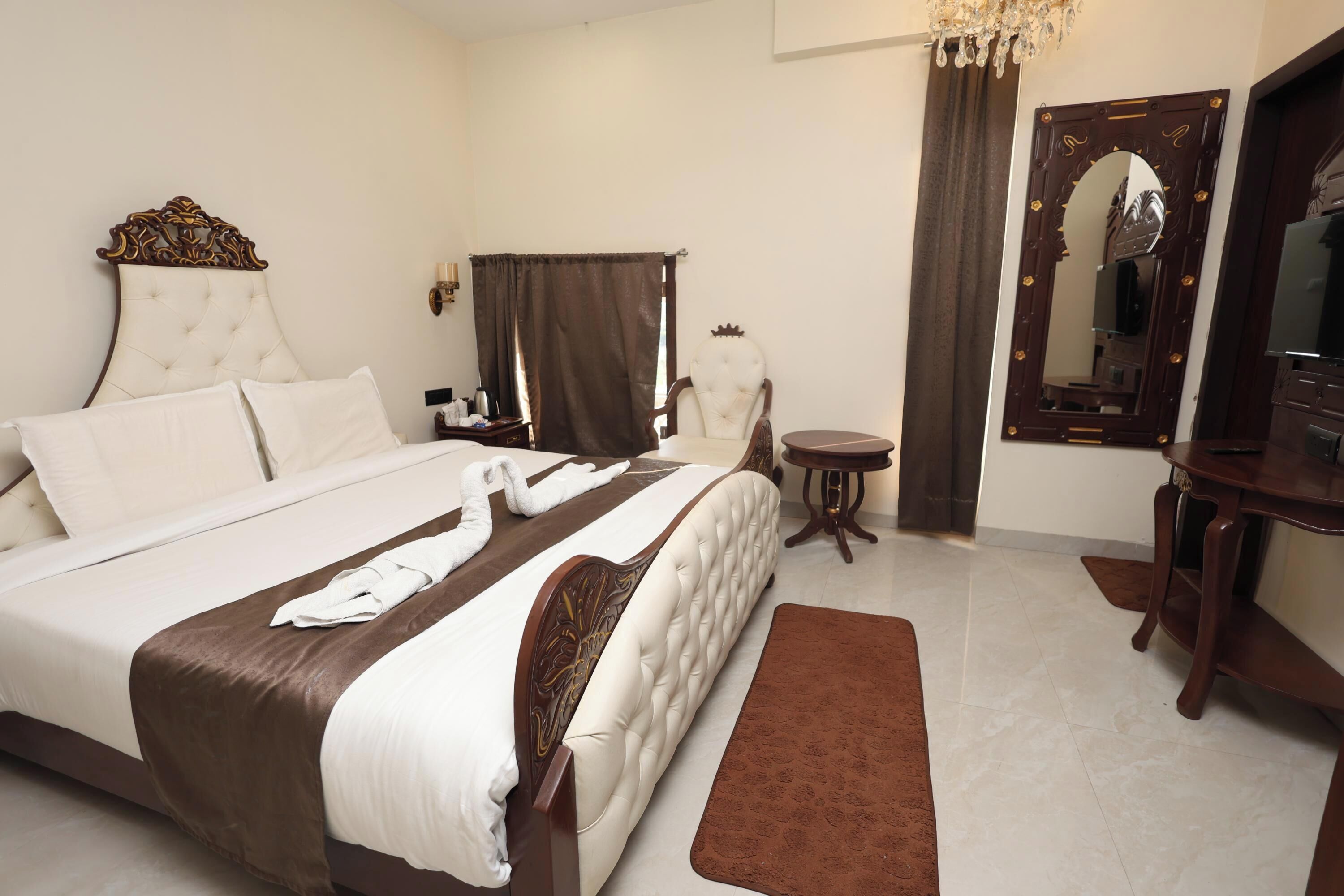 Quarto de hotel com uma cama grande, uma cadeira, uma mesa pequena e um espelho.