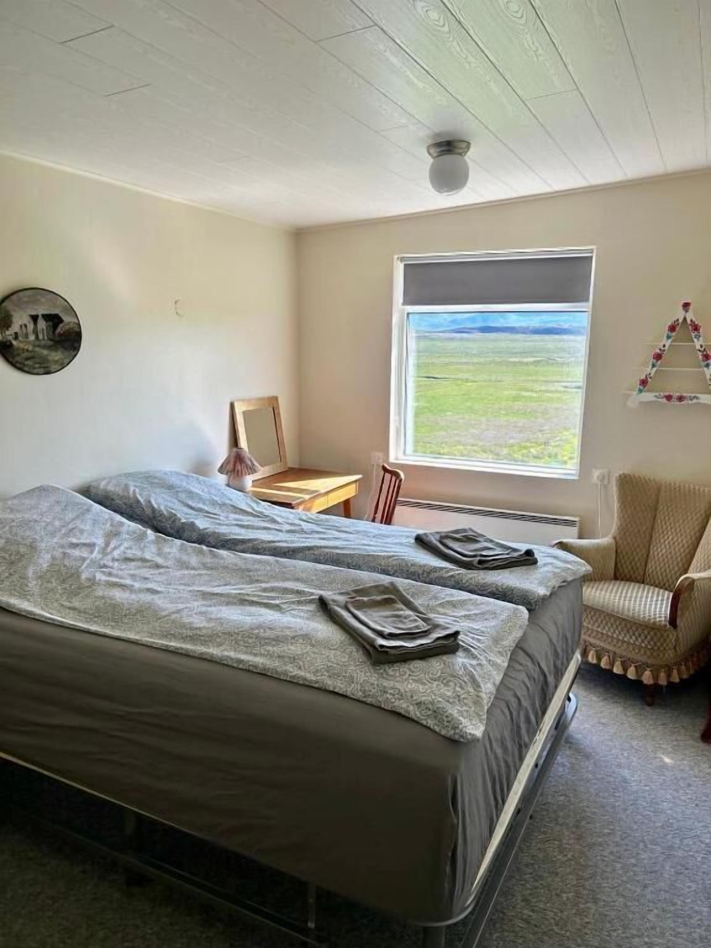 Quarto com duas camas, uma escrivaninha, uma cadeira e uma janela grande com vista.