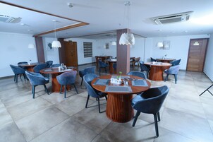 Uma sala de conferências ampla, com várias mesas e cadeiras, equipada com luminárias modernas e aparelhos de ar condicionado.