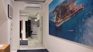 Um corredor com um grande mural panorâmico de vista para o mar, uma secretária de madeira e um tapete azul escuro.