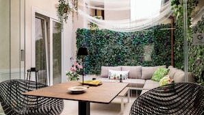 Uma sala de estar moderna com um sofá, duas cadeiras de vime preto, uma mesa de madeira e uma parede coberta por folhagem verde.